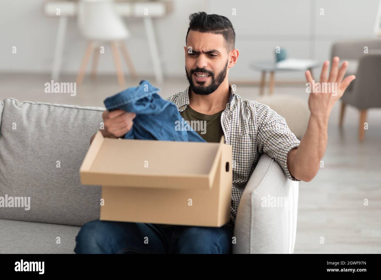 Disappointed young Arab guy unboxing carton package, receiving clothes ...