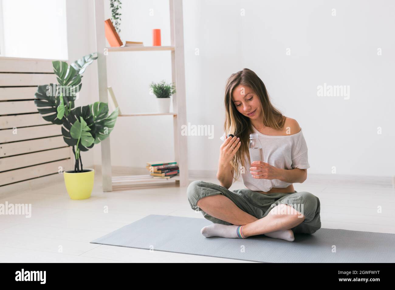 Young beautiful girl practicing yoga at mat, drinking water while break ...
