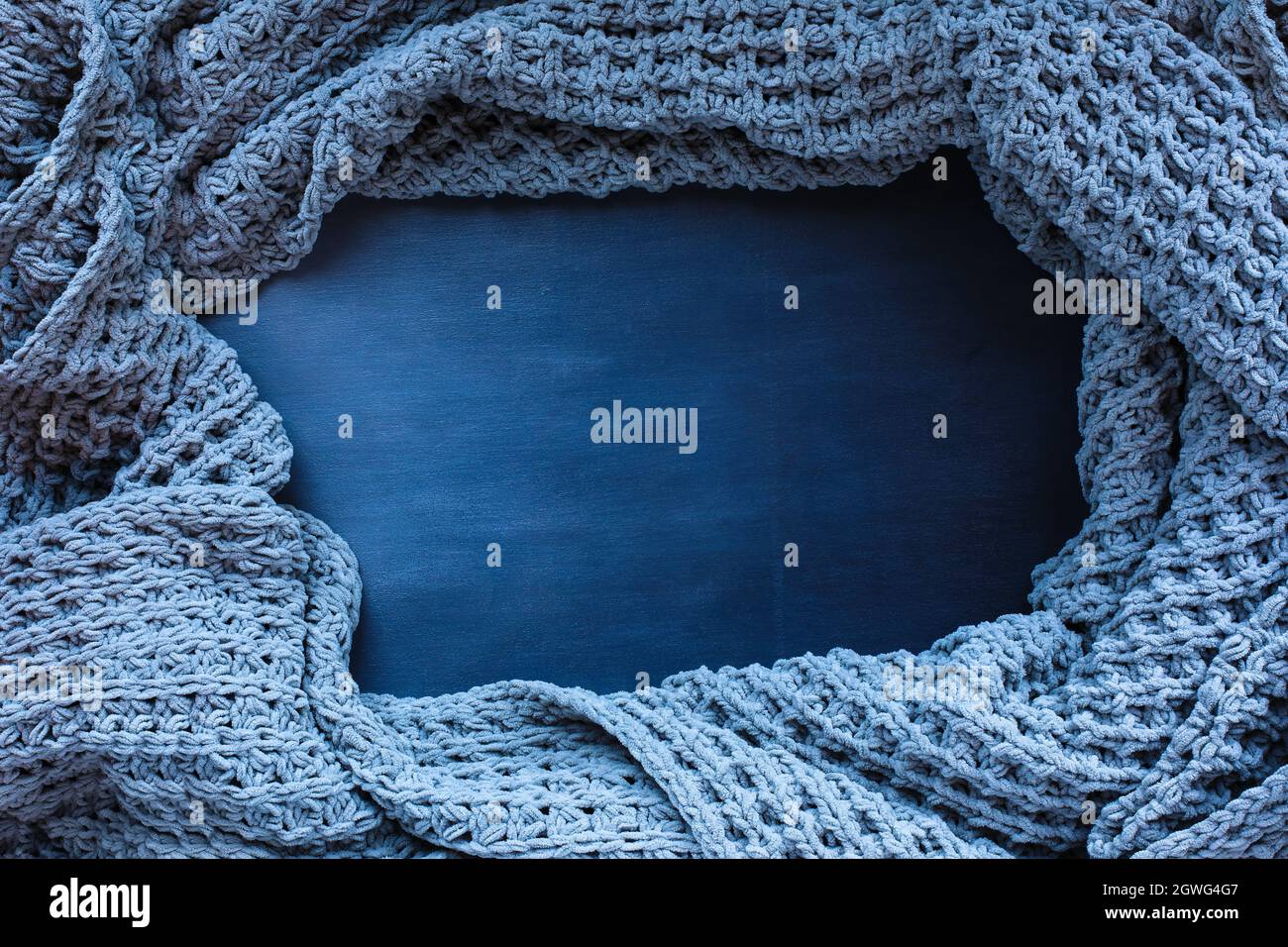 Grey woven blanket crumpled and framed over a blue toned black wooden ...
