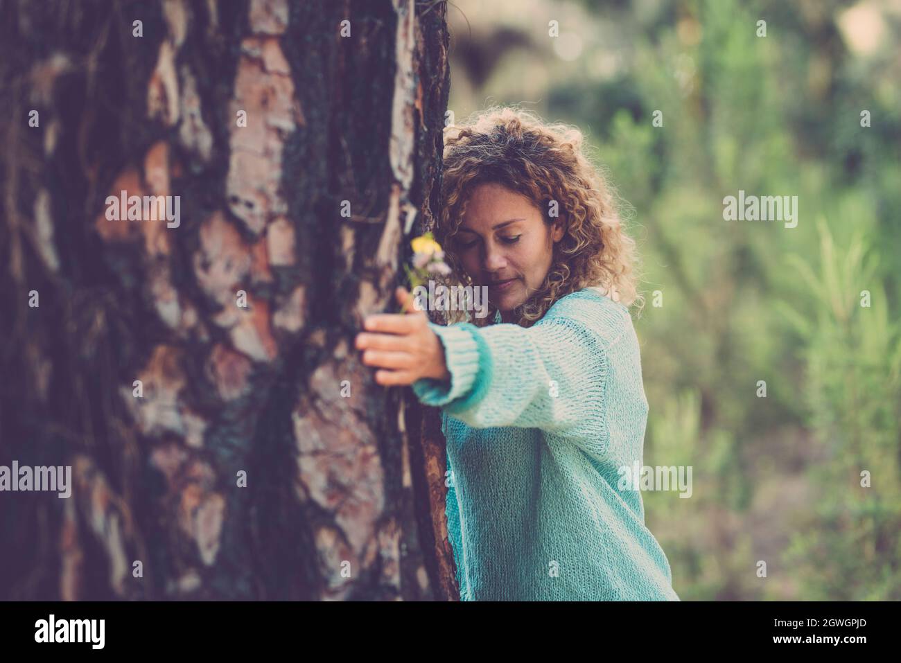 Young woman hugging tree with eyes closed in forest. Beautiful ...