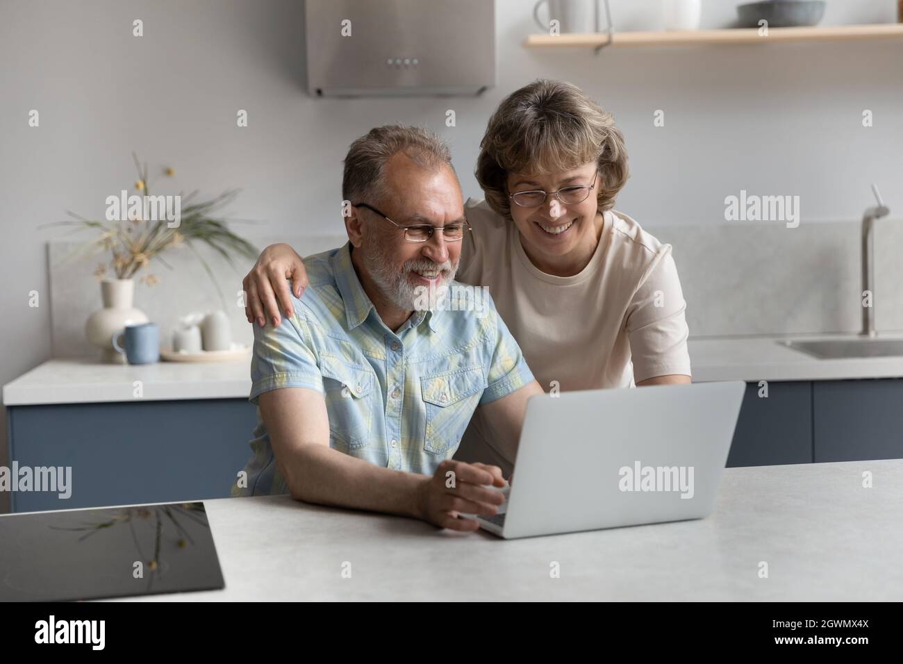 Happy middle aged couple using computer in kitchen Stock Photo - Alamy