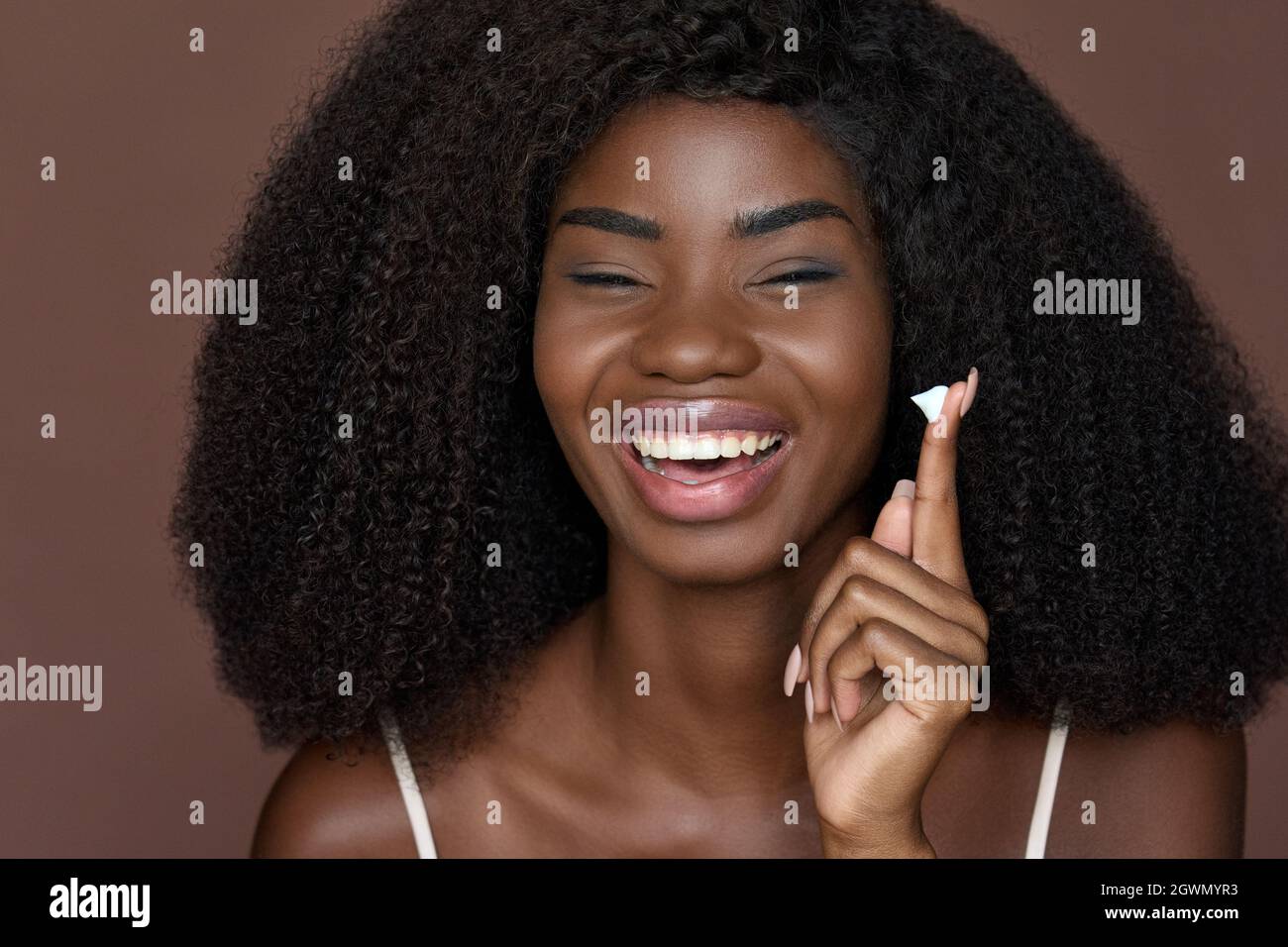Happy young black woman applying facial cream isolated on brown ...