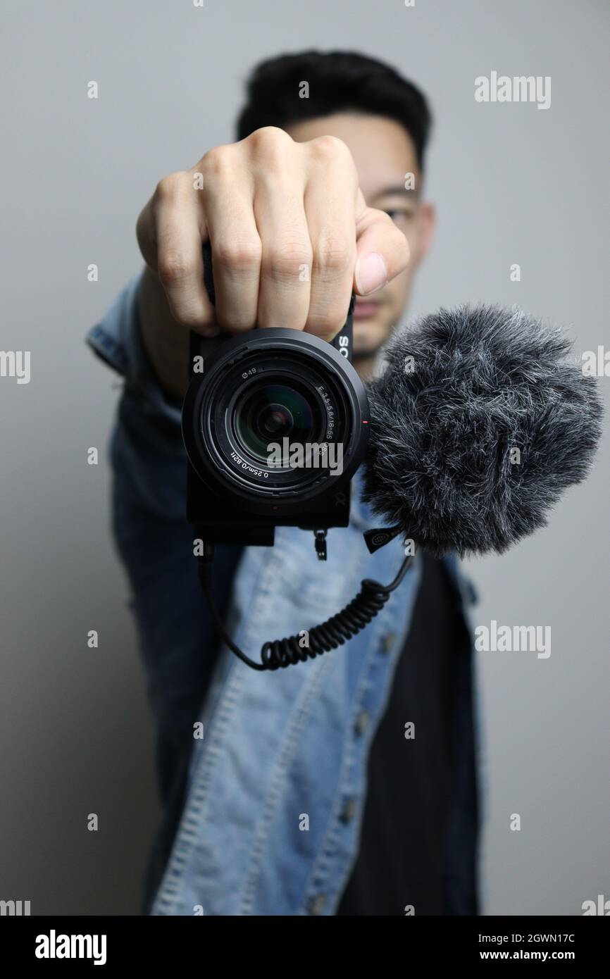 A vertical shot of an adult man holding a DSLR camera with a microphone ...