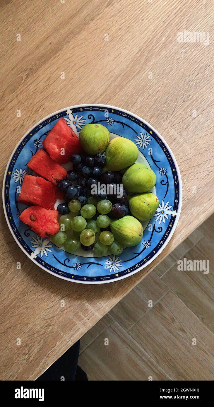 A vertical shot of ripe figs, watermelon cubes, and berries on a plate ...
