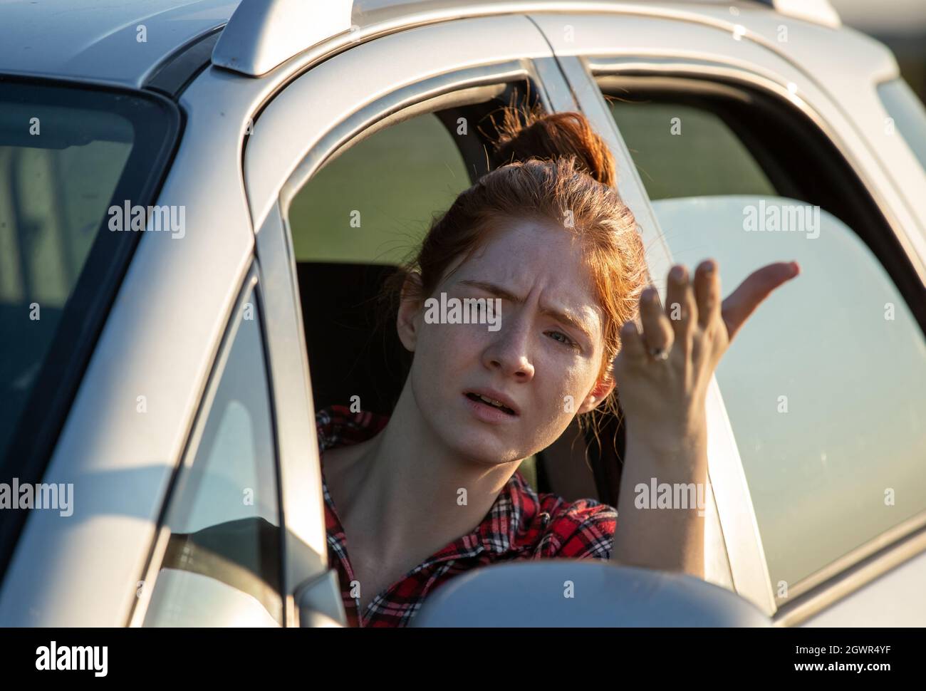 Young redhead gesturing with hand through window of car. Frustrated ...
