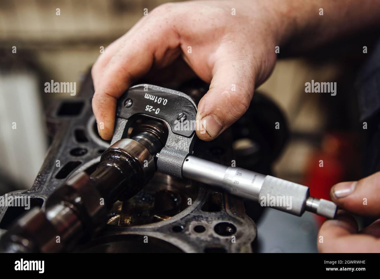a measuring device in hand measures the camshaft against the background ...