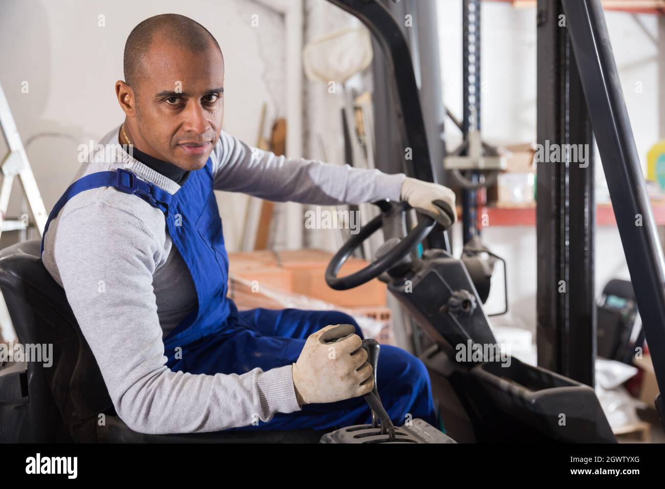 Confident hispanic worker driving forklift in building materials store ...