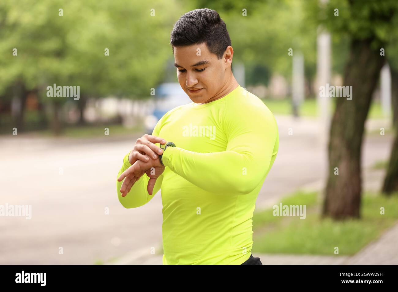 Muscular young man looking at wristwatch in park Stock Photo - Alamy