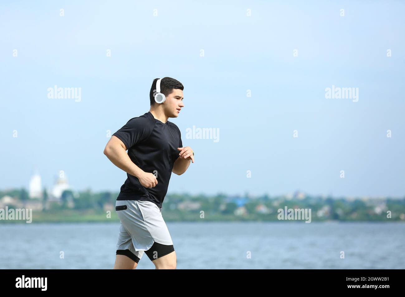 Muscular young man in headphones running near river Stock Photo - Alamy