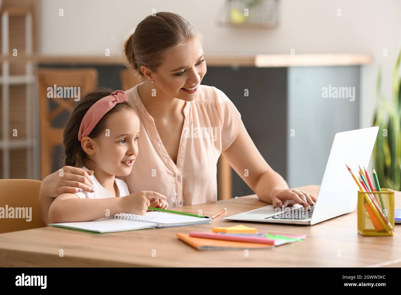 Little girl with her mother doing lessons online at home Stock Photo ...