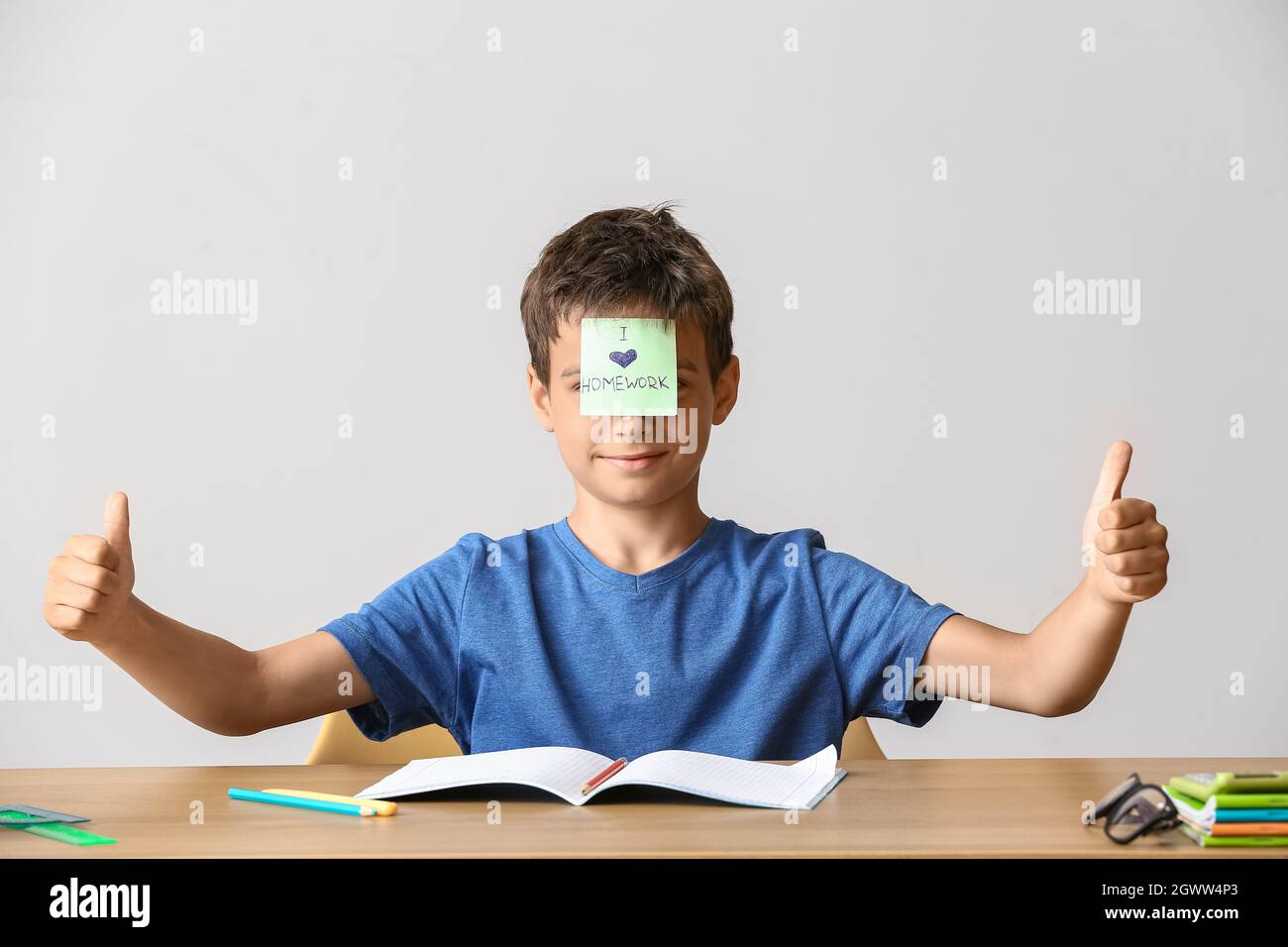 Little boy with sticker on his forehead showing thumbs-up at table on ...