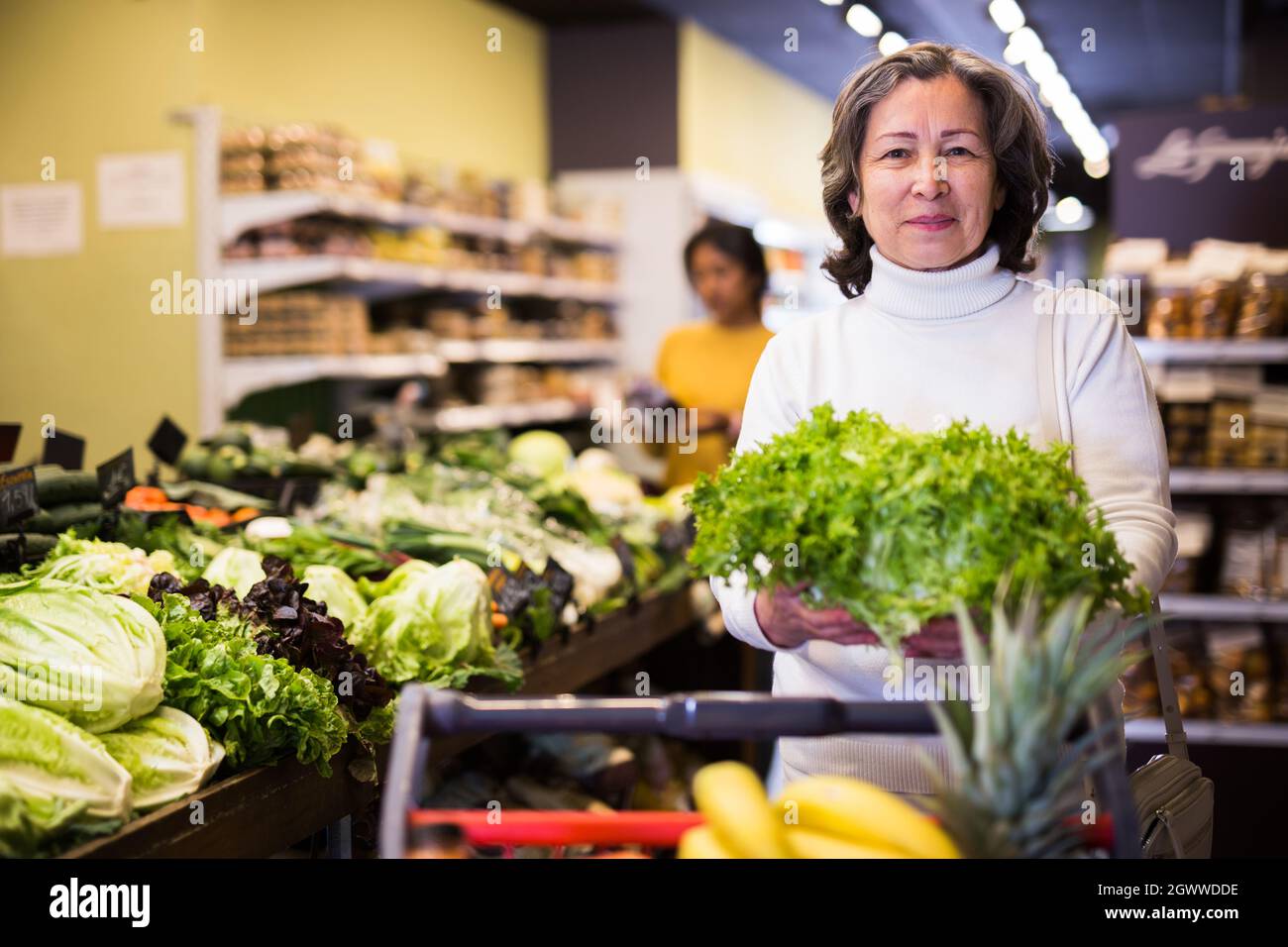 Happy elderly female purchaser with green frisee lettuce in supermarket ...