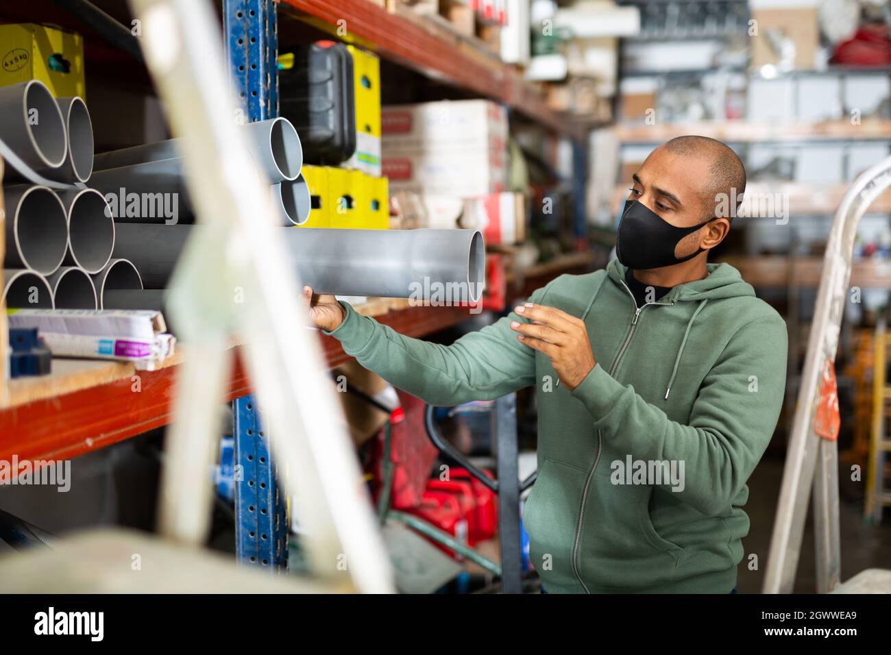 Craftsman in protective mask selects plastic plumbing pipes in hardware ...