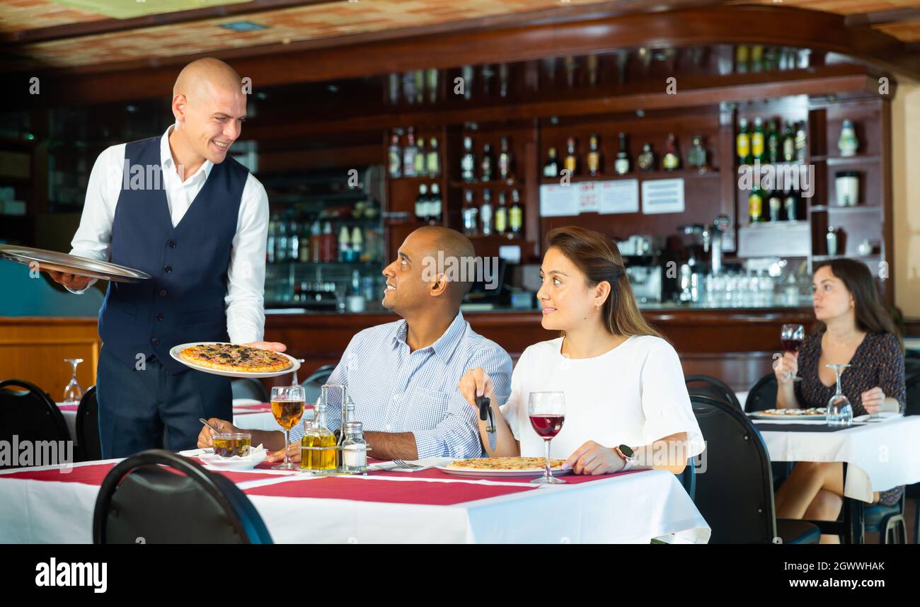 Smiling waiter serving delicious pizza to couple in restaurant Stock ...