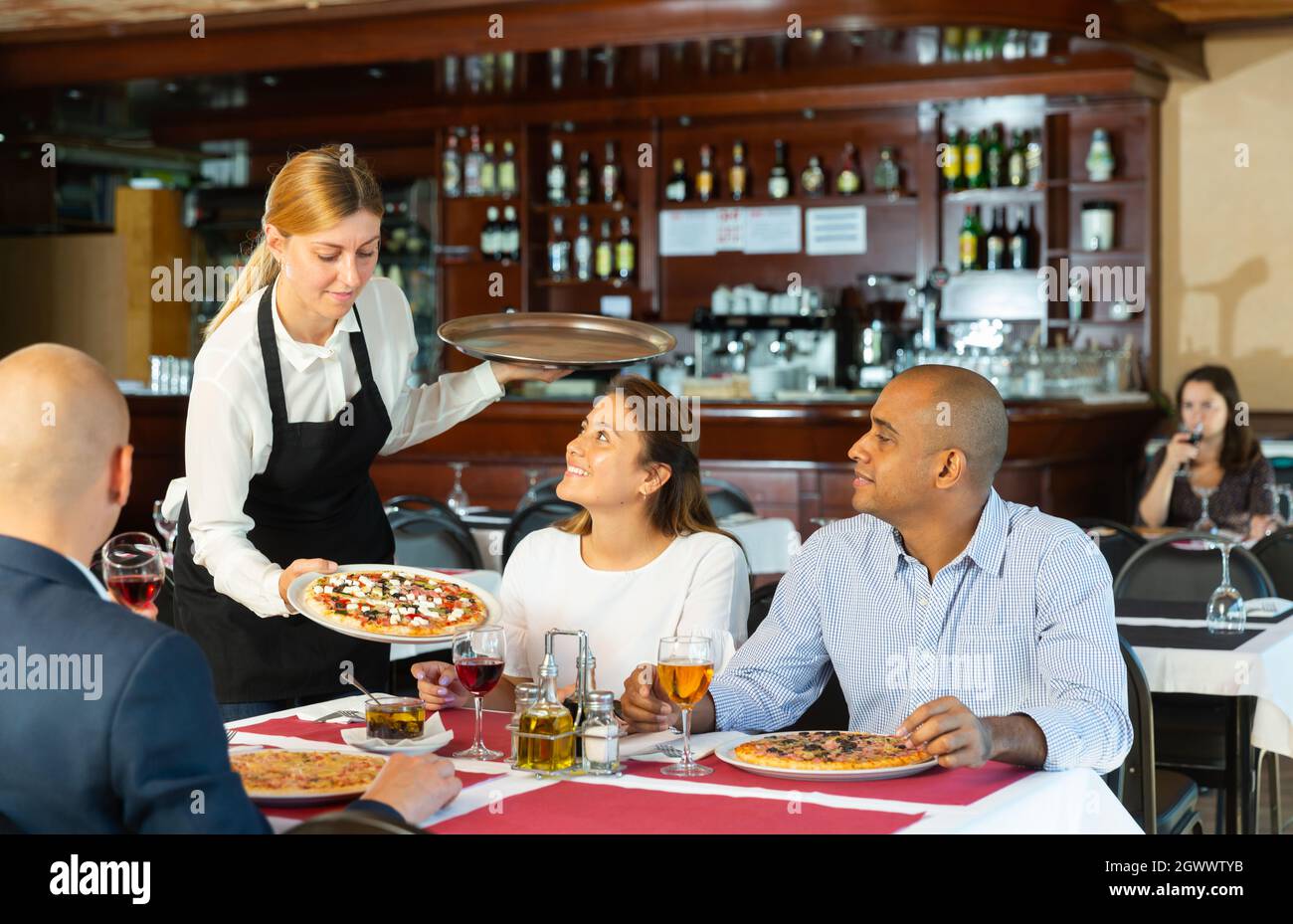 Young waitress serving ordered pizza to guests in restaurant Stock ...