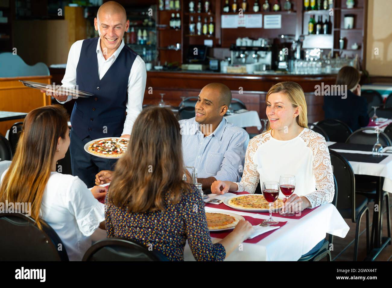 Polite waiter bringing pizza to friends in restaurant Stock Photo - Alamy