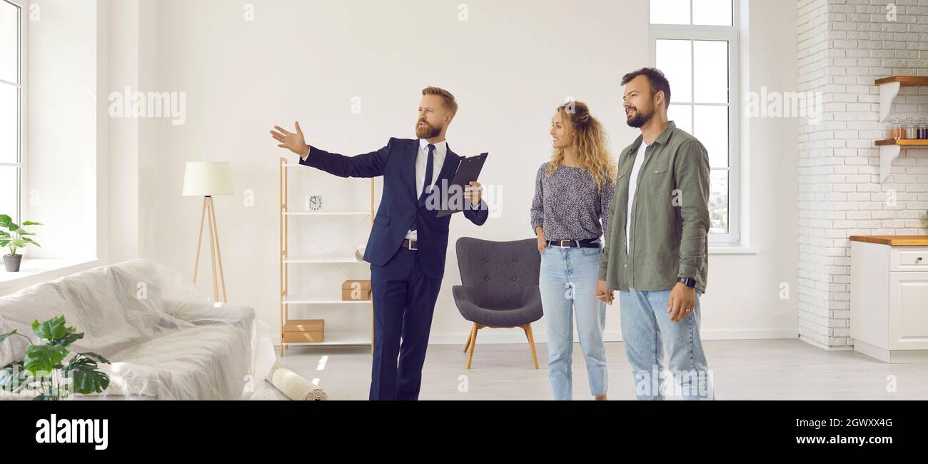 Real estate agent giving young customers tour about rooms in new house ...