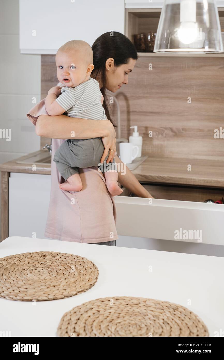 Busy mother cleaning kitchen with baby on her arms. Woman cooking and ...