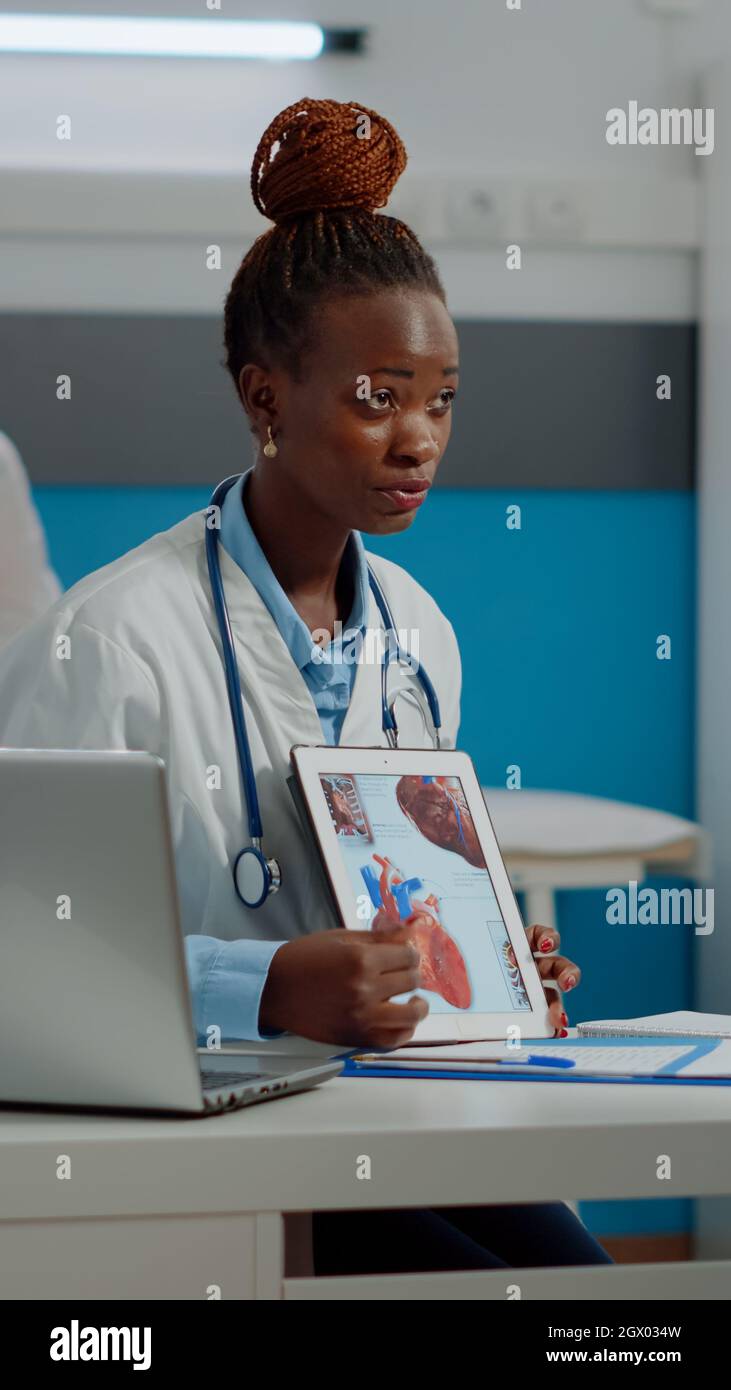 Young medic holding tablet with medical cardiogram sitting at desk in ...