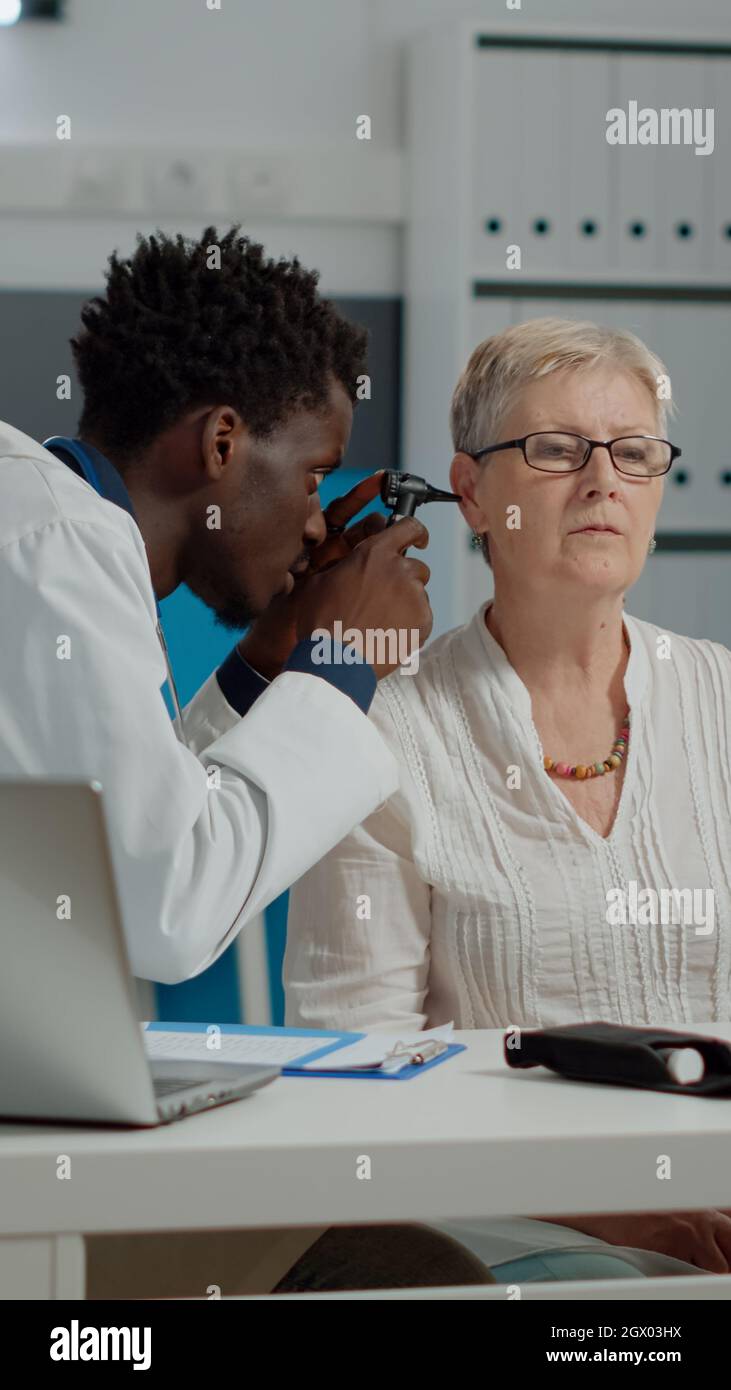 Young doctor using otoscope for ear checkup in cabinet with senior ...