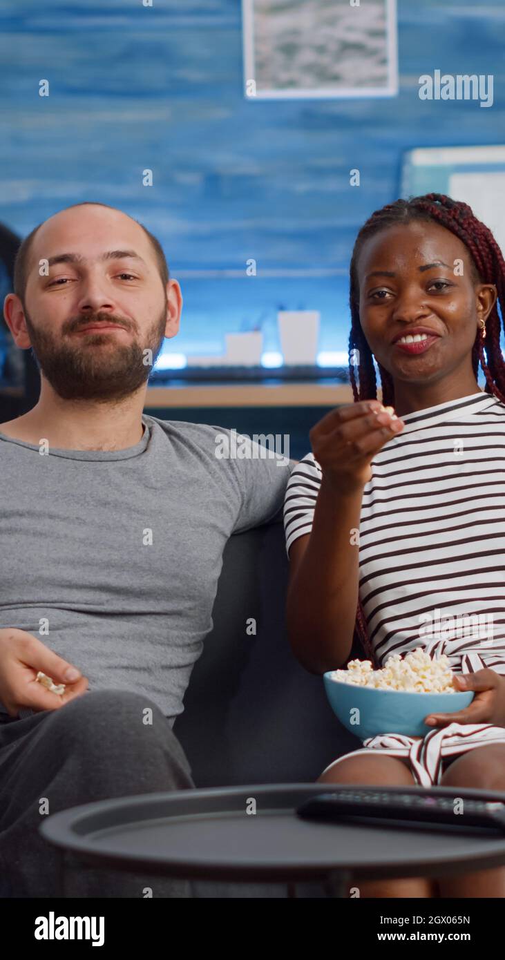 Young interracial couple watching movie on TV with popcorn sitting in ...
