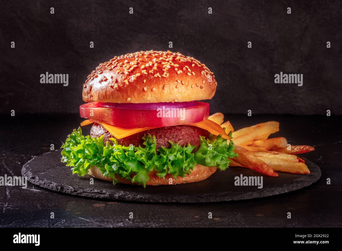 Classic beef burger with French fries, a side view on a black ...