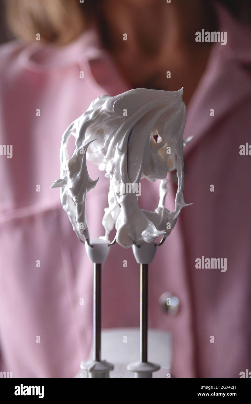 Whisk with whipped egg white in female confectioner hand on pink suit ...