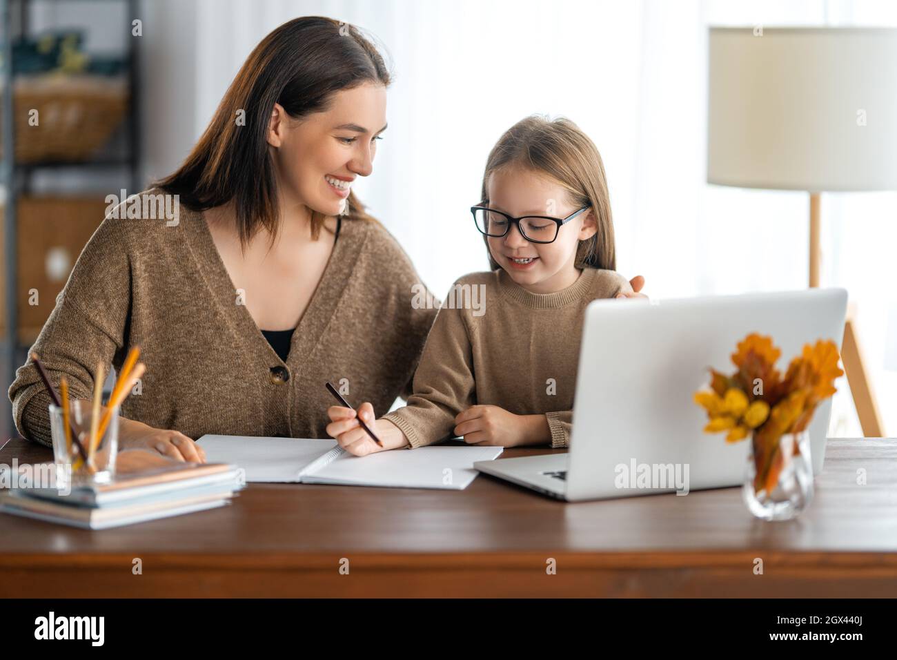 Back to school. Happy child and adult are sitting at desk. Girl doing ...