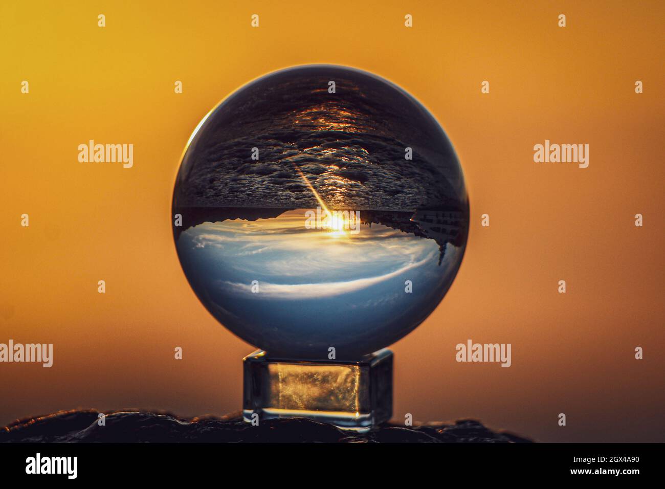 Glass ball with reflection of sunset by the beach on an orange ...