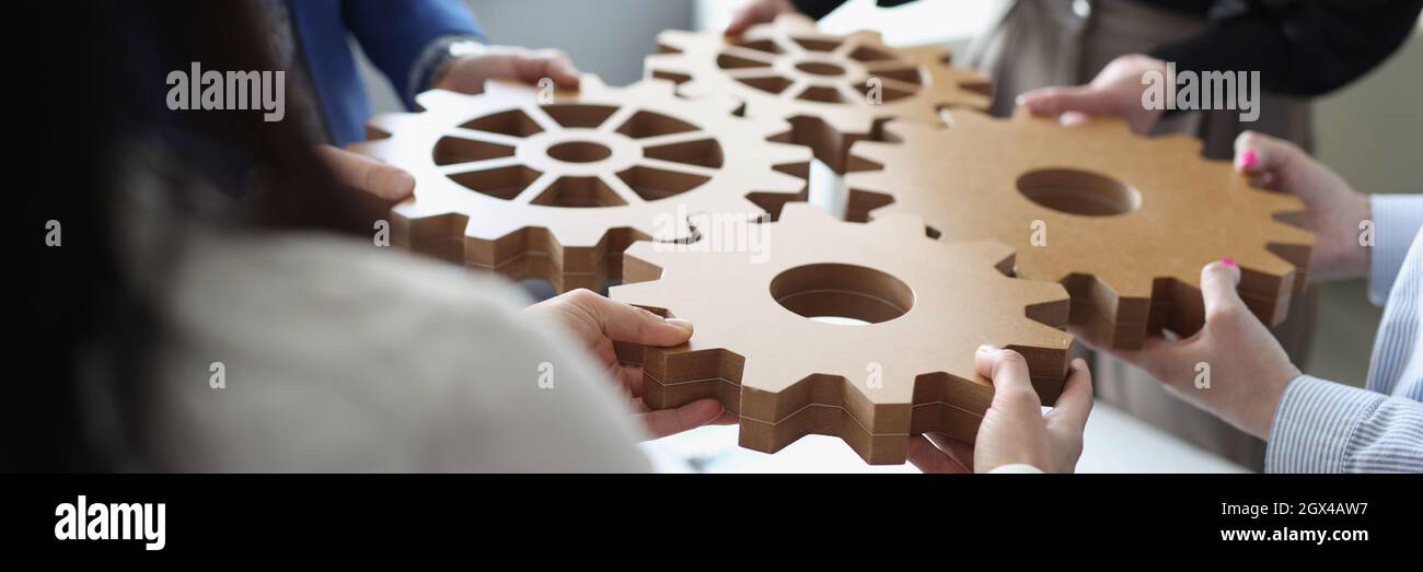 Efficient business team connects wooden gears into one Stock Photo - Alamy