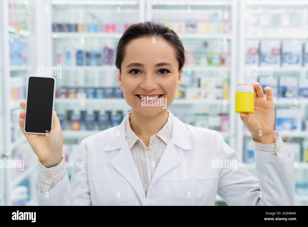cheerful pharmacist in white coat holding smartphone with blank screen ...