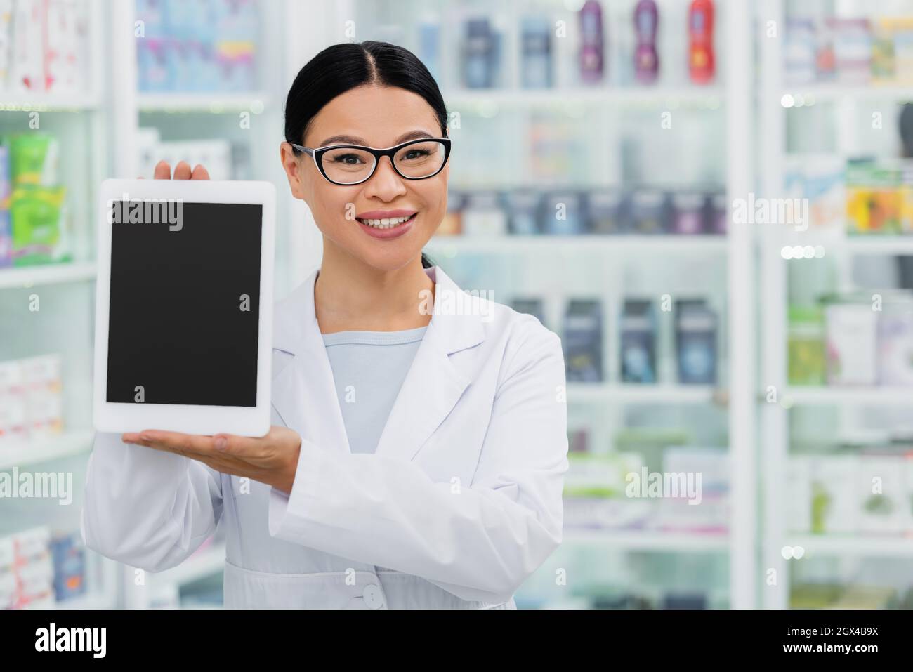 positive asian pharmacist in glasses holding digital tablet with blank ...