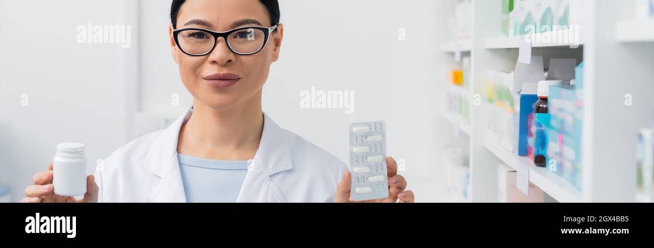 pleased asian pharmacist holding bottle and blister pack with ...