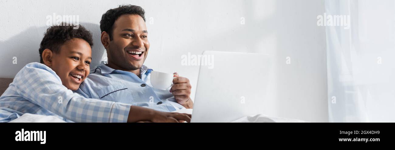 laughing african american boy pointing at laptop while watching movie ...