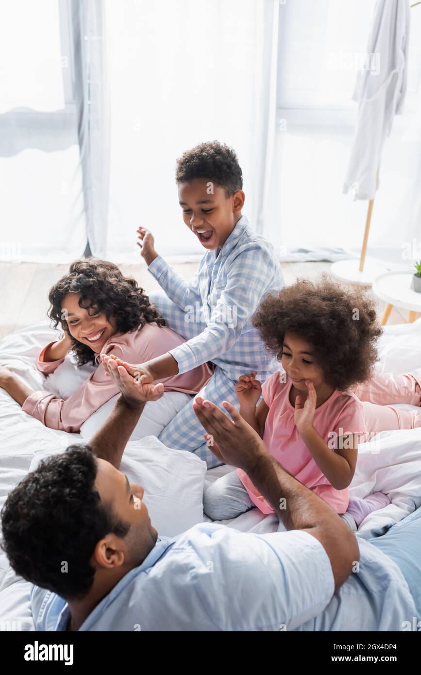 african american man playing patty cake game with kids in bed near ...