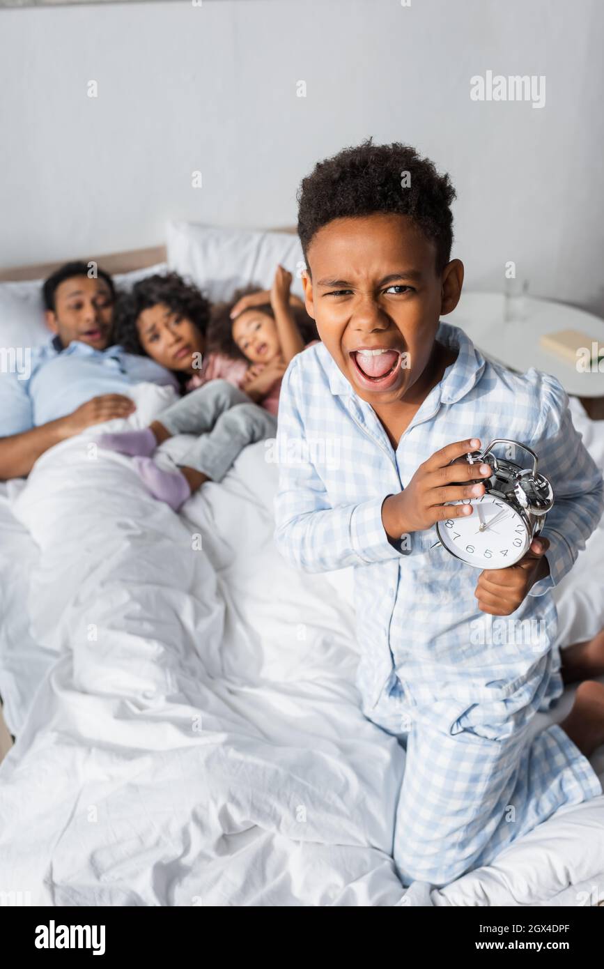 thrilled african american boy with alarm clock shouting near blurred ...