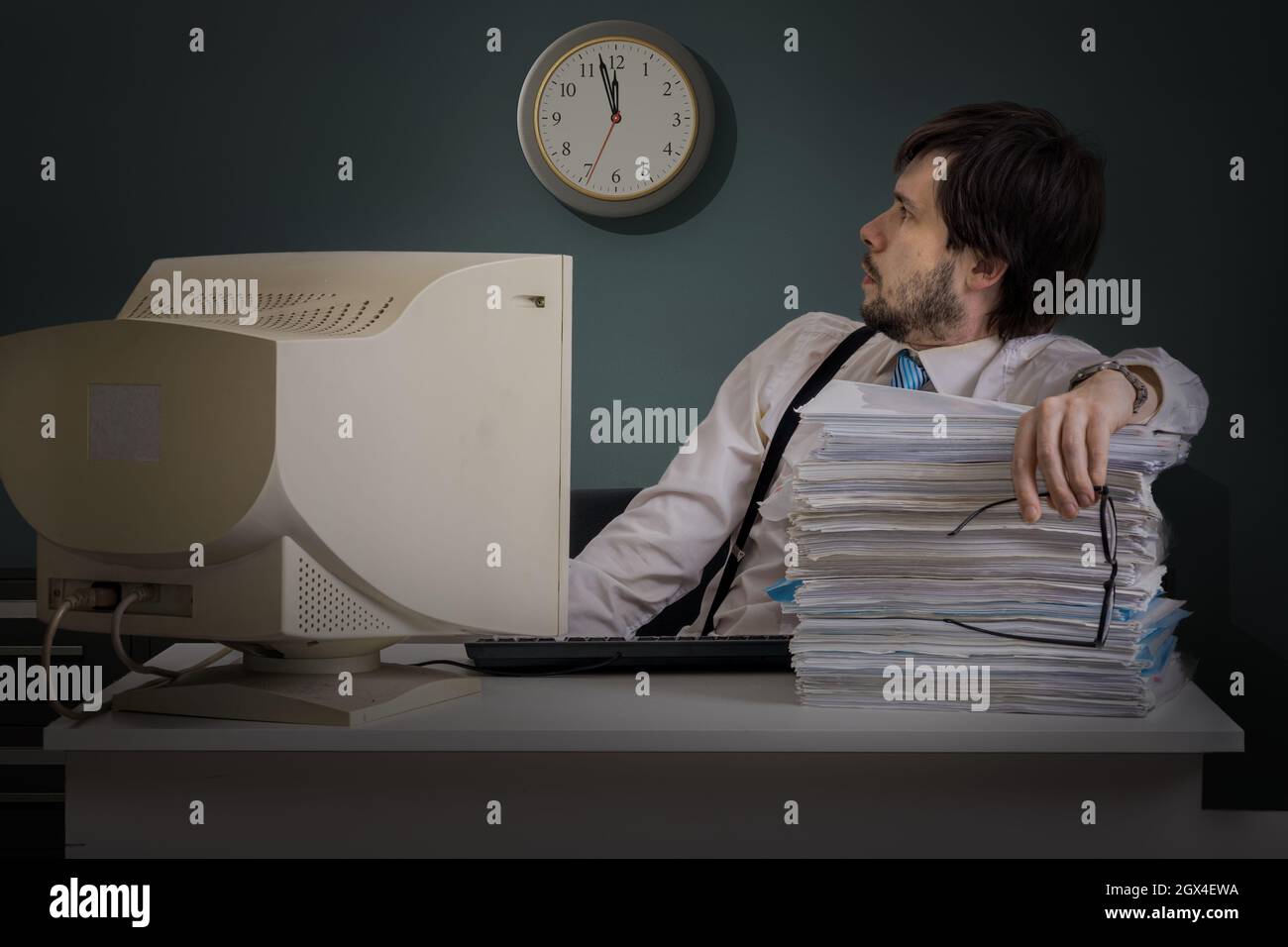 Tired man is looking on clock in office at night. Overwork concept ...