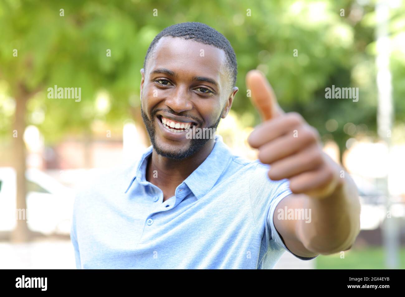 Happy black man gesturing thumbs up looking at camera in a park Stock ...