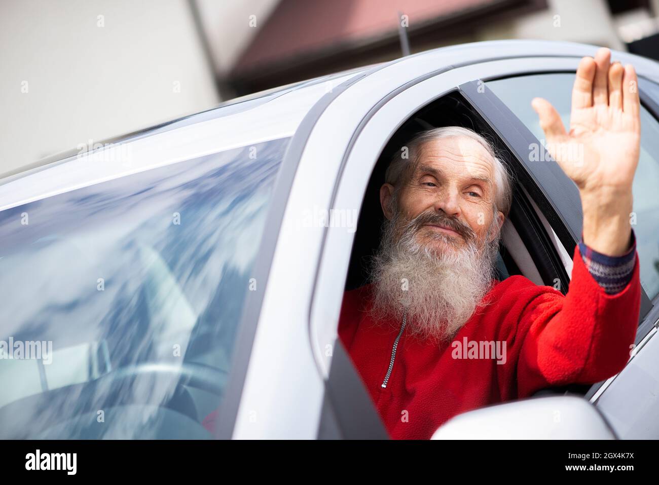 Sad face bearded senior man waving hand through window of gray car ...