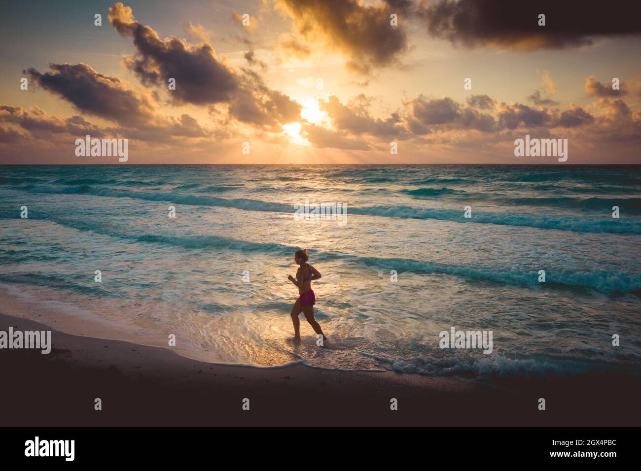 Silhouette of a female running across the beach on a sunrise Stock ...