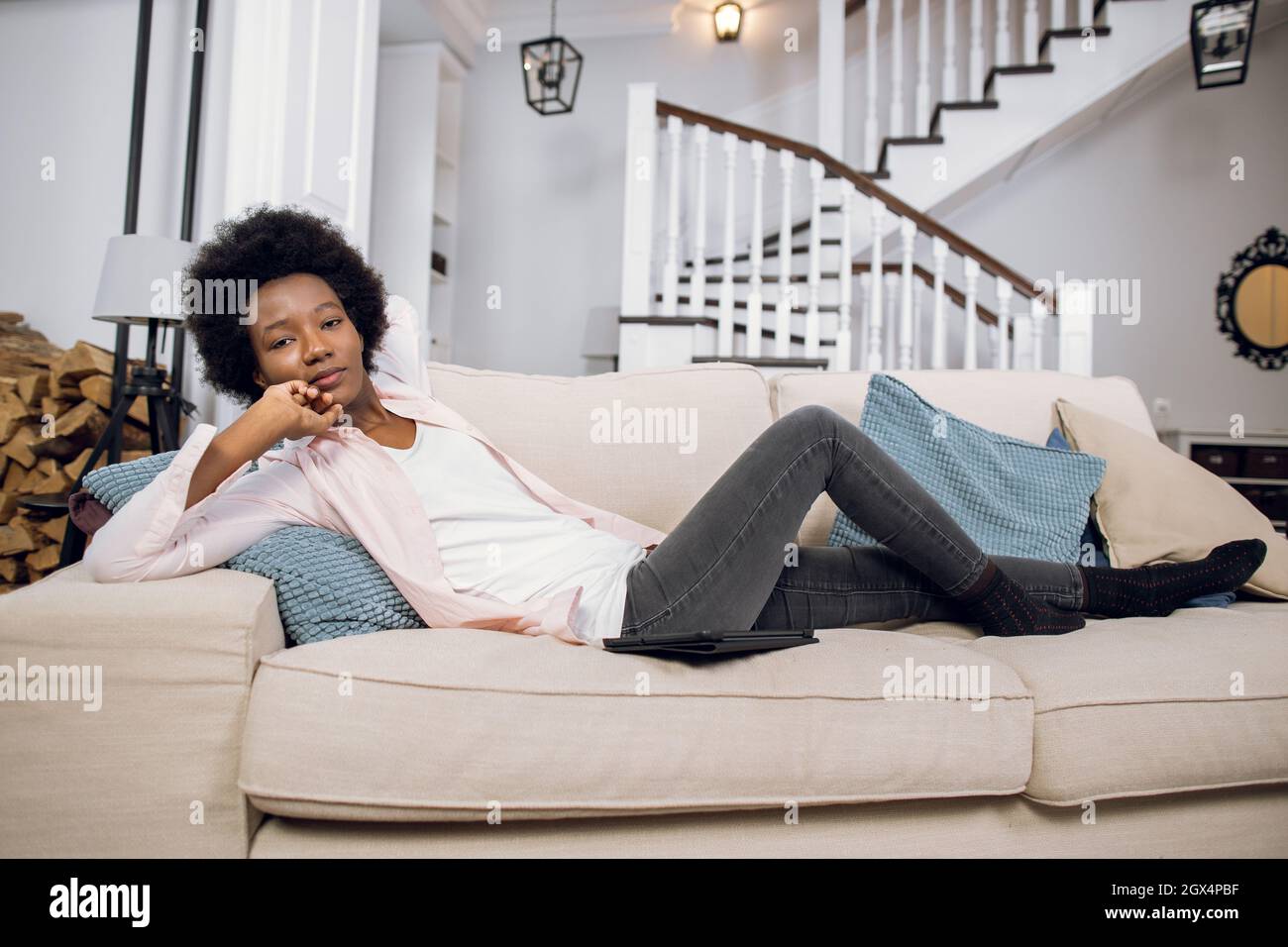 Pretty african woman in casual clothes lying on couch with digital ...