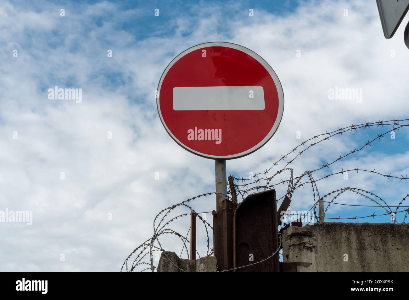 No entry road sign is located on a concrete fence with barbed wire ...