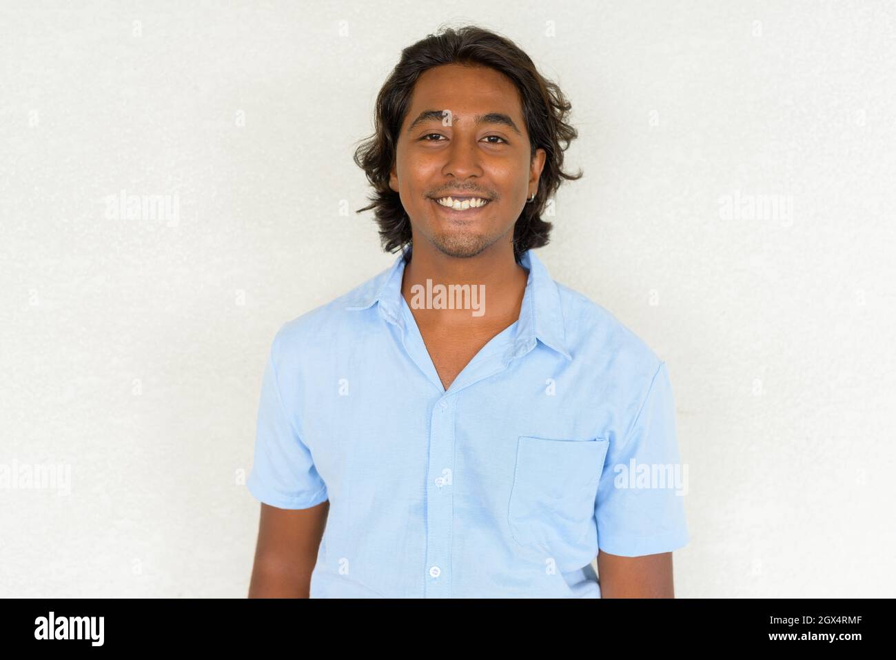 Portrait of handsome young Indian man against plain background outdoors ...