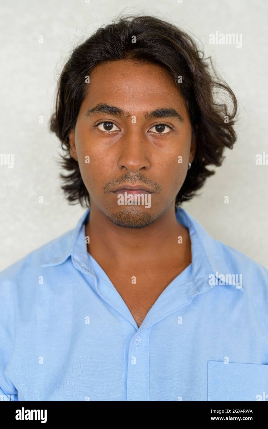 Portrait of handsome young Indian man against plain background outdoors ...