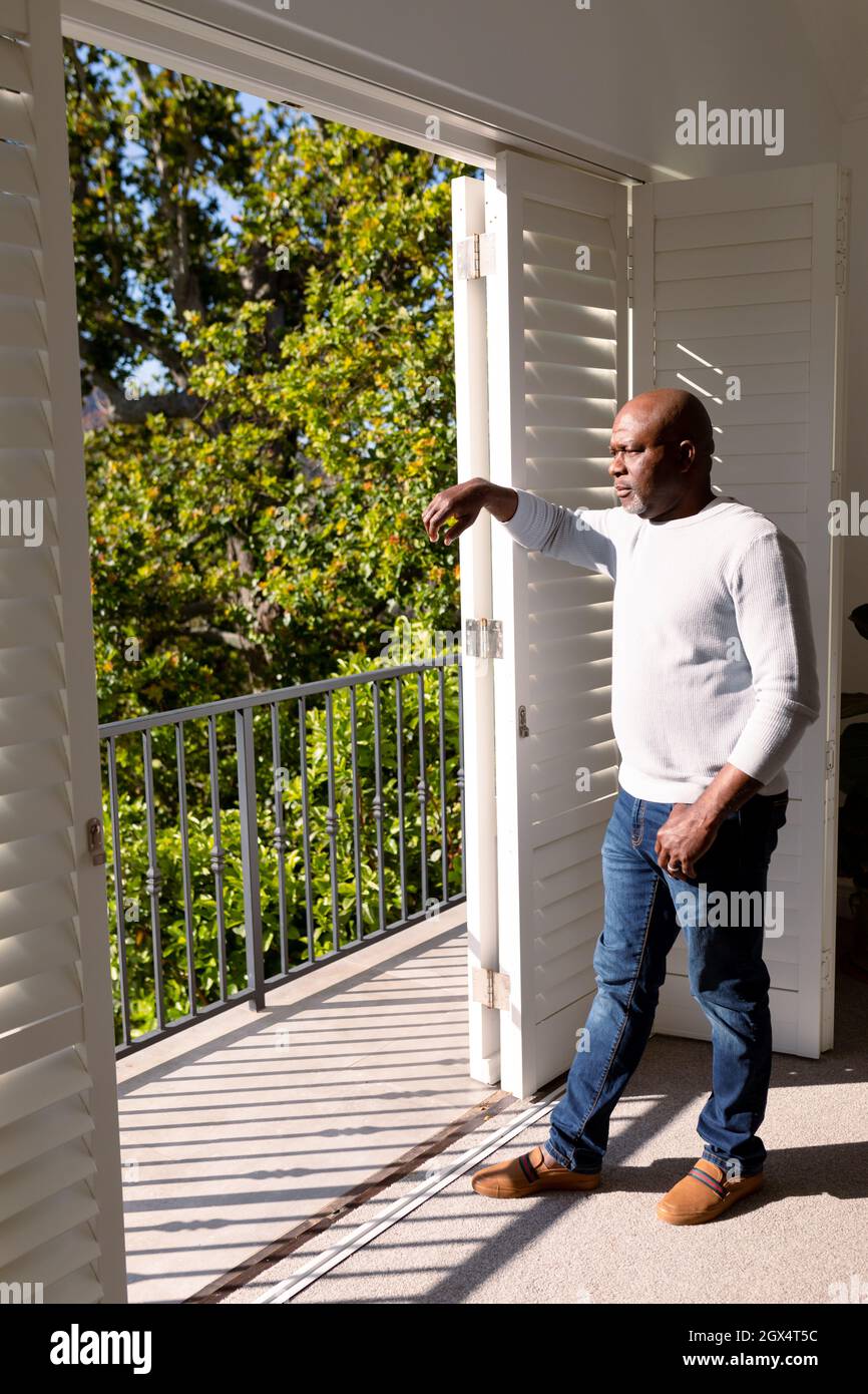 Thoughtful african american senior man standing at window and looking ...