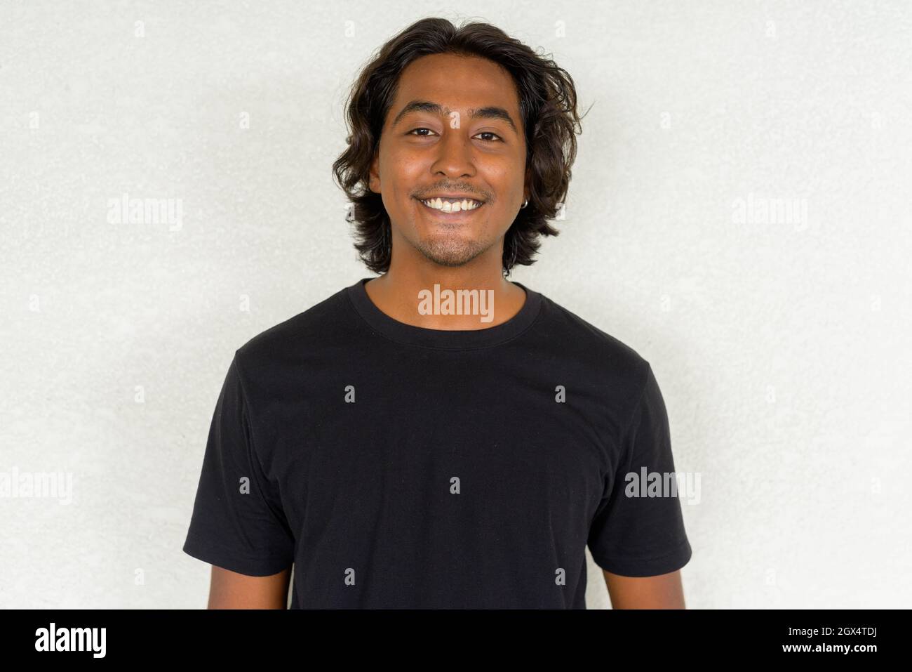 Portrait of handsome young Indian man against plain background outdoors ...
