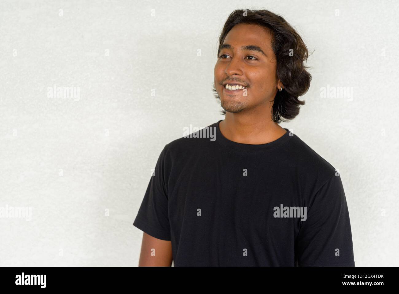 Portrait of handsome young Indian man against plain background outdoors ...