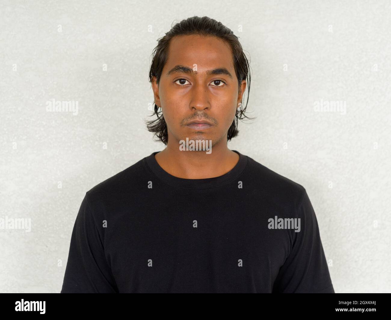 Portrait of handsome young Indian man against plain background outdoors ...