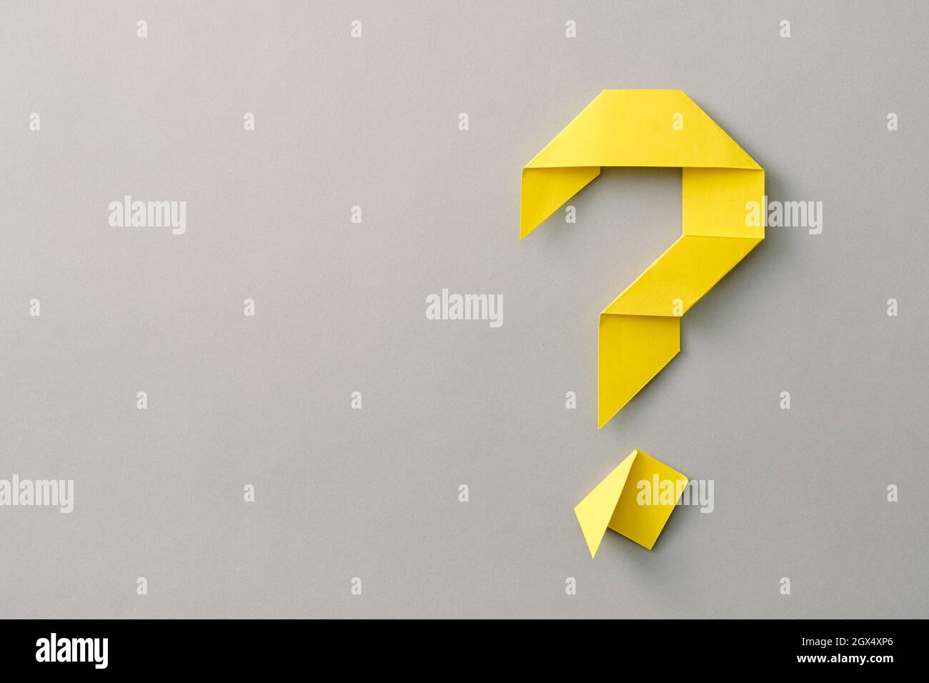 Decorative yellow paper origami question mark on grey with copy space ...