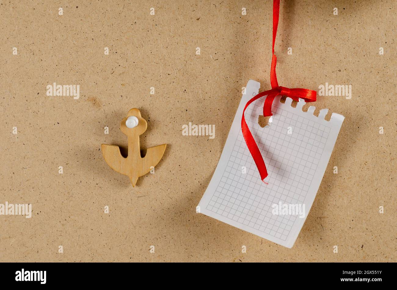 Wooden anchor. A sheet of paper hanging from a thin red ribbon ...